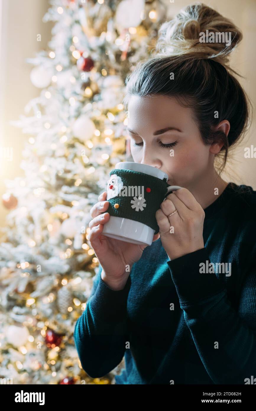 Woman drinking from holiday mug in front of christmas tree Stock Photo ...