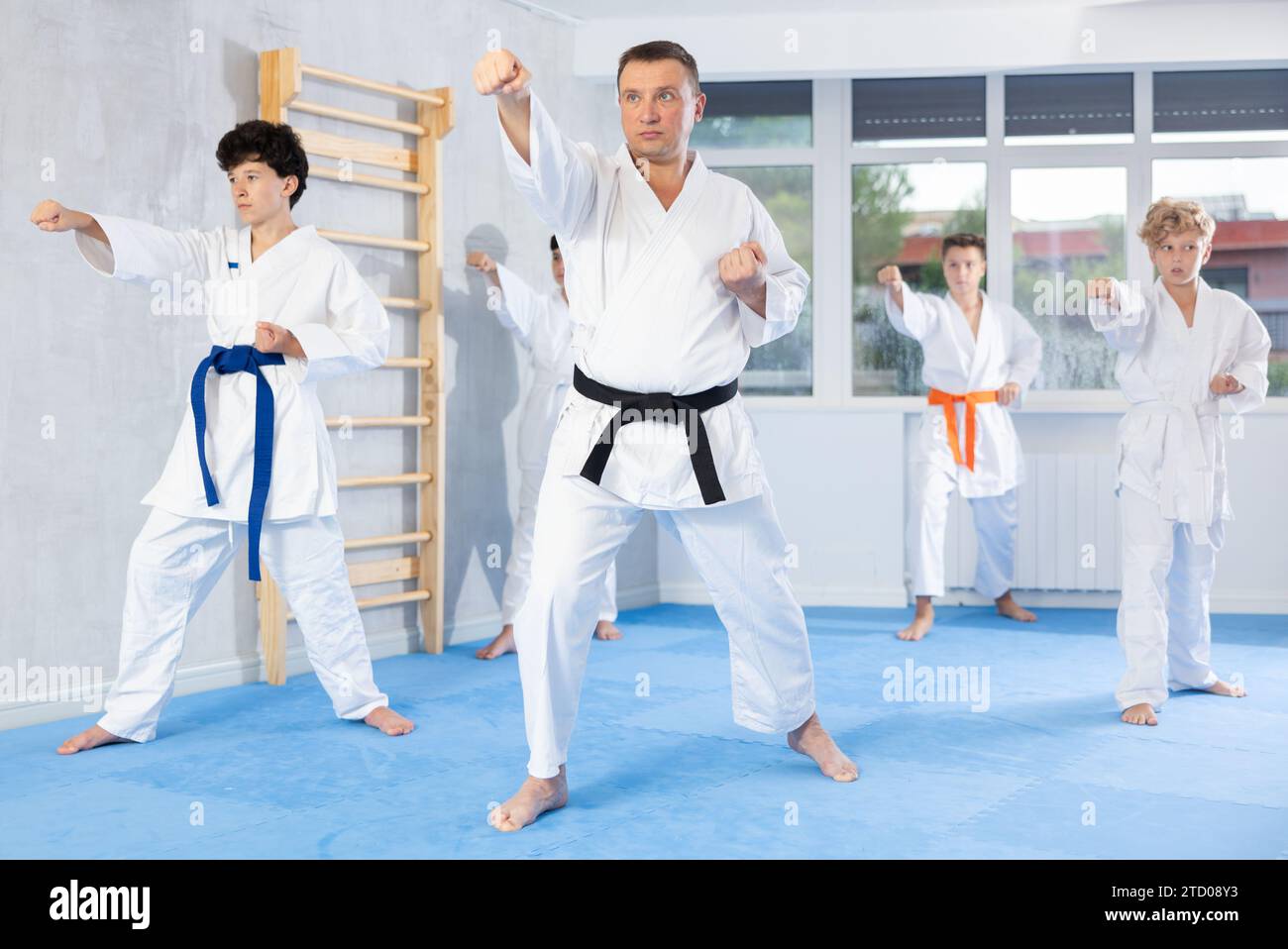 Middle-aged trainer practicing kata standing in row with preteen ...