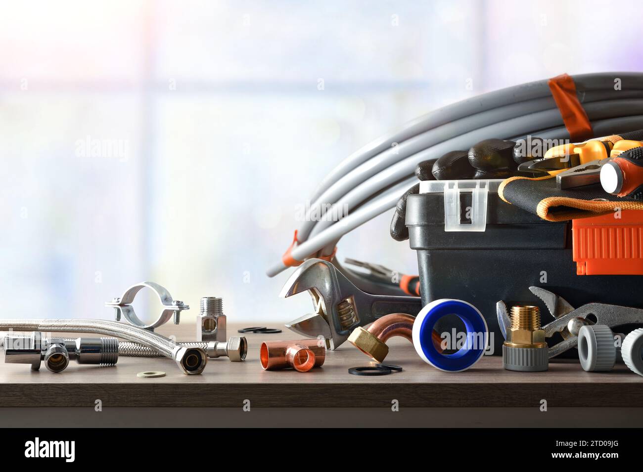 Plumber's toolbox with material around on wooden table with window in background. Front view ...