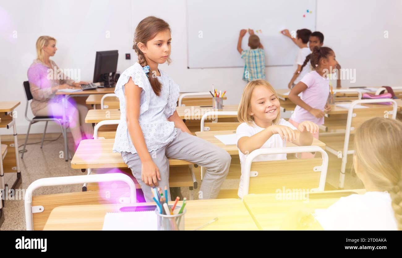 Positive primary school students are talking about homework at desk ...