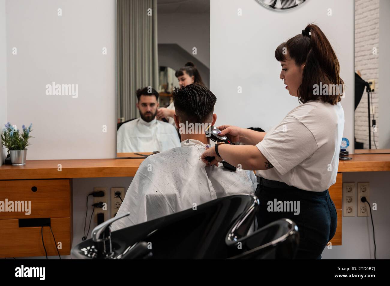 Side view of focused female hairstylist using electric trimmer on male ...