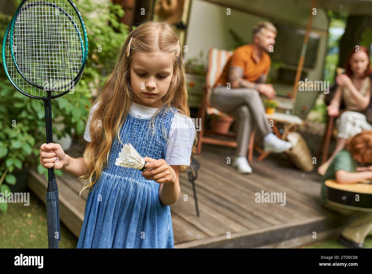 girl holding badminton rockets and shuttlecock near family and trailer ...