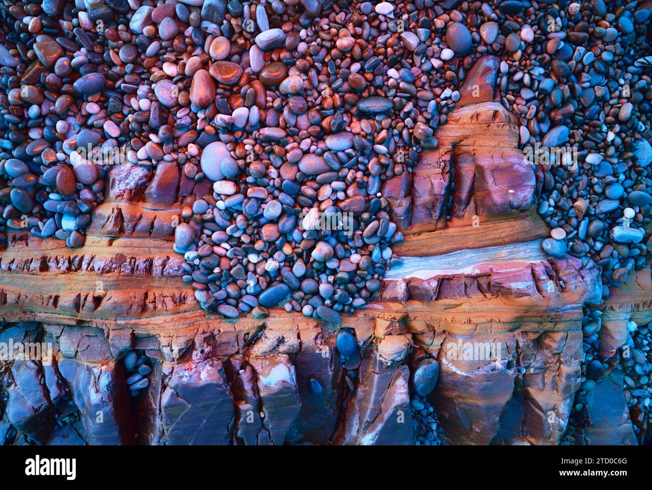 Vibrant pebbles scattered over a striking, layered sedimentary rock ...