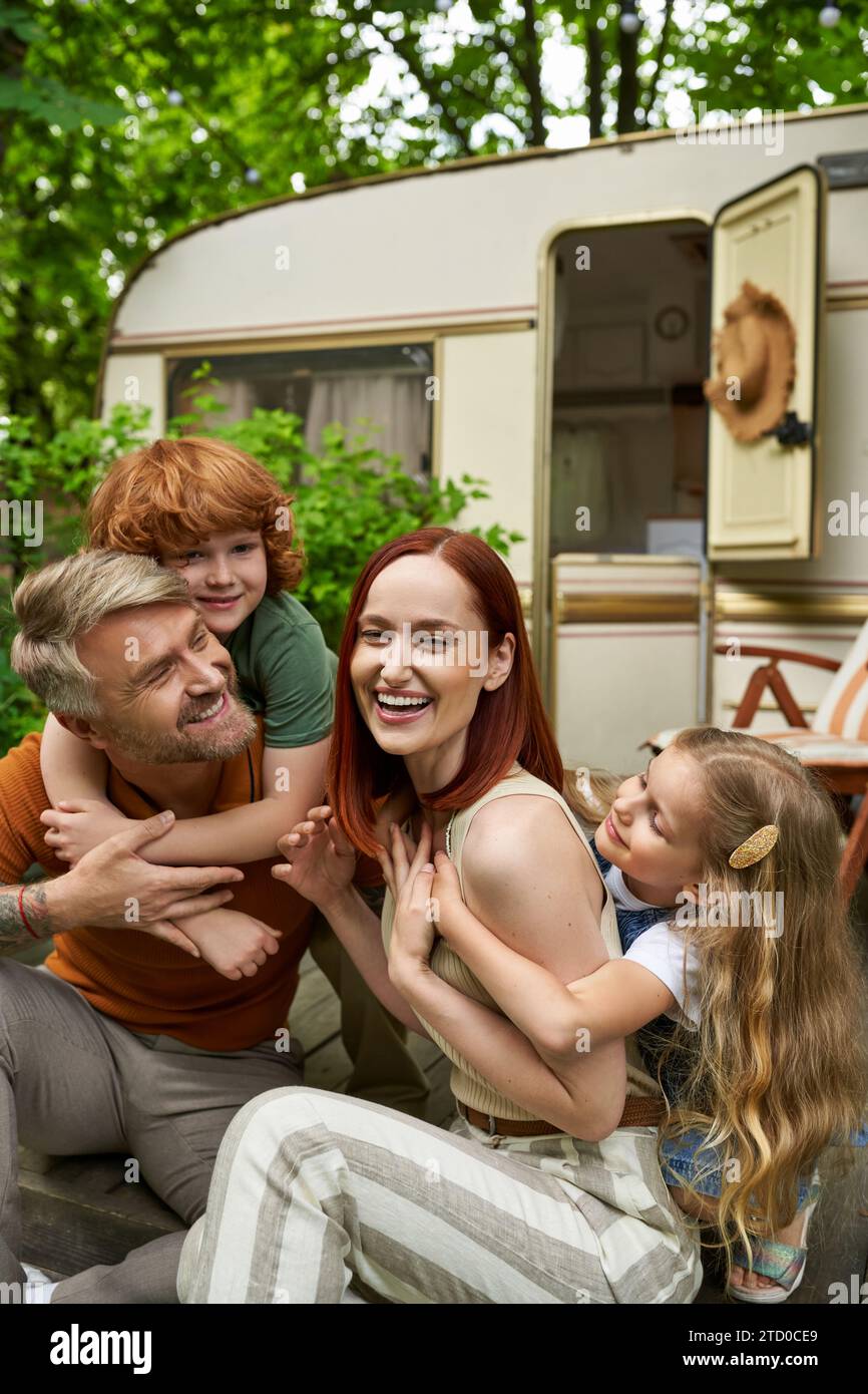 cheerful children embracing laughing parents sitting at trailer home ...