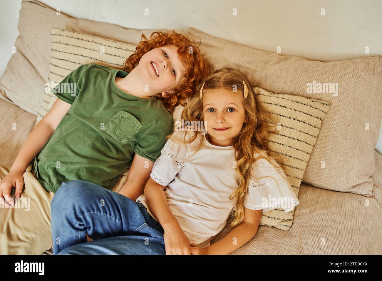 top view of brother and sister lying on bed with soft pillows and ...