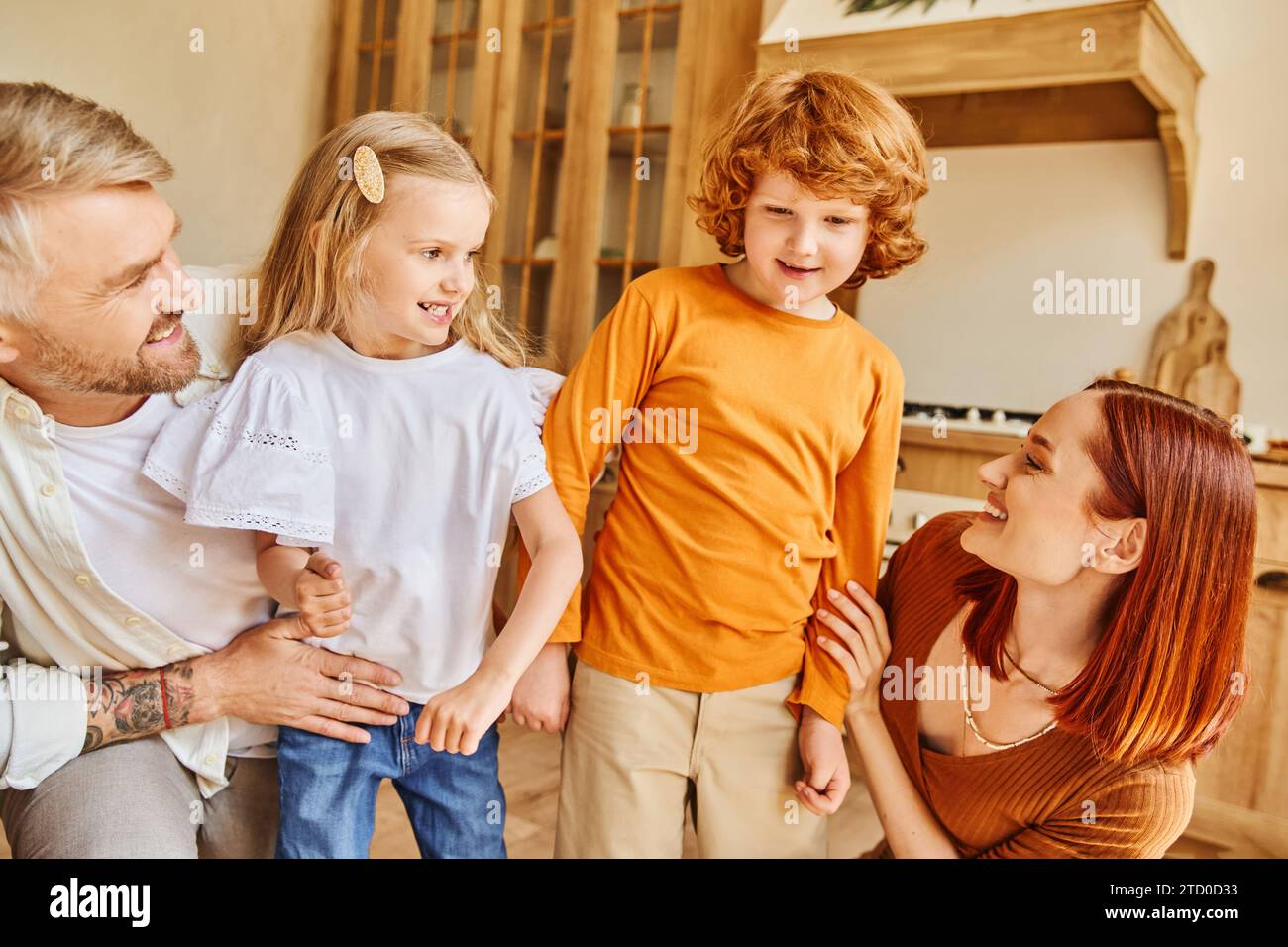 cheerful parents embracing excited daughter and son in cozy kitchen at ...