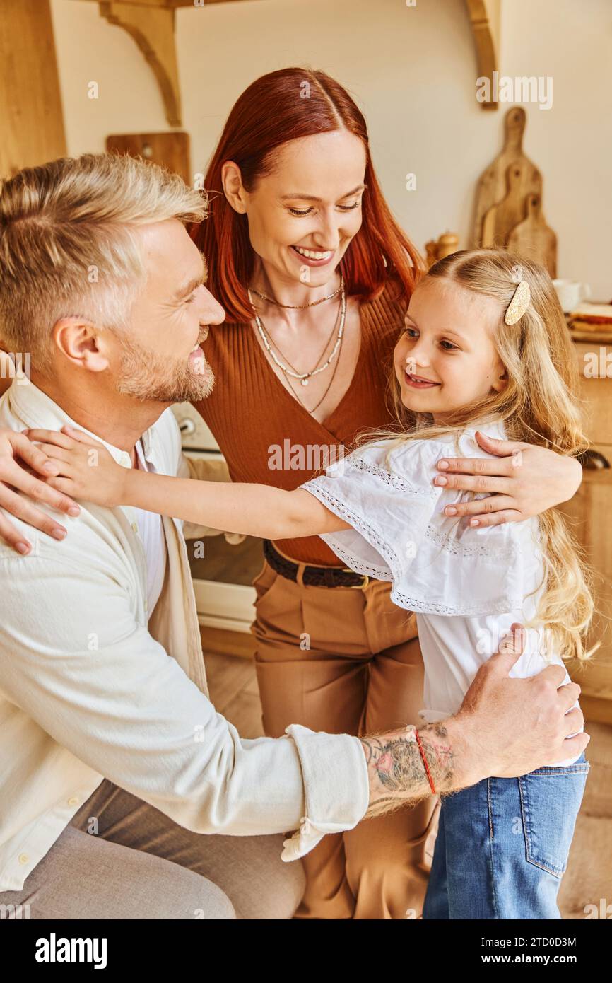 caring parents with adorable daughter embracing in cozy kitchen at home ...