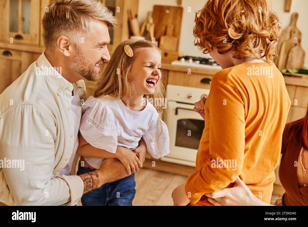parents tickling overjoyed children and having fun in modern kitchen at ...