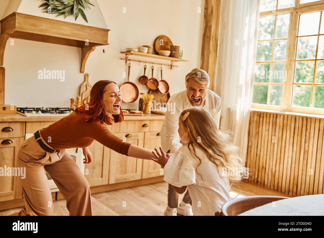 overjoyed parents playing with cute daughter in modern kitchen at home ...