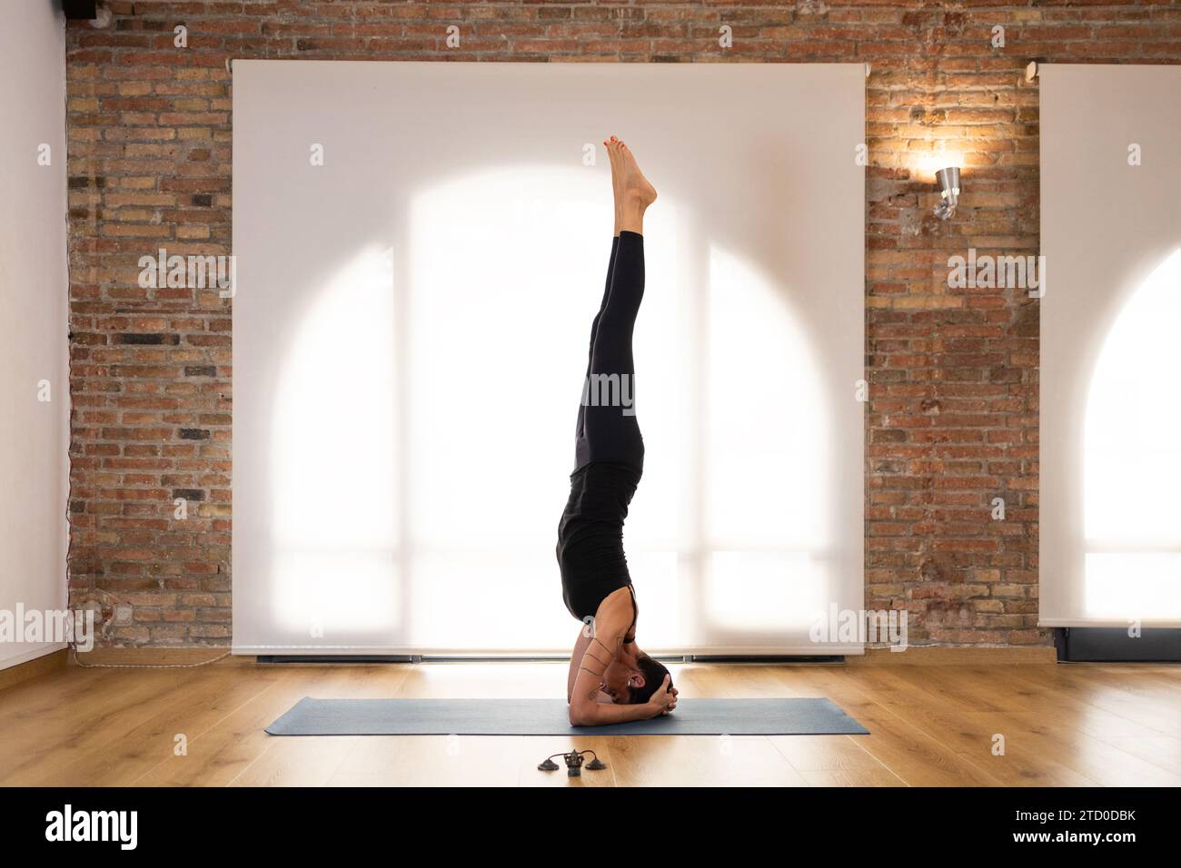 A woman executing a headstand yoga pose on a mat in a bright, loft ...