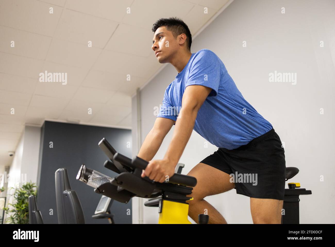 A focused young adult male cycling on an exercise bike in a well-lit ...