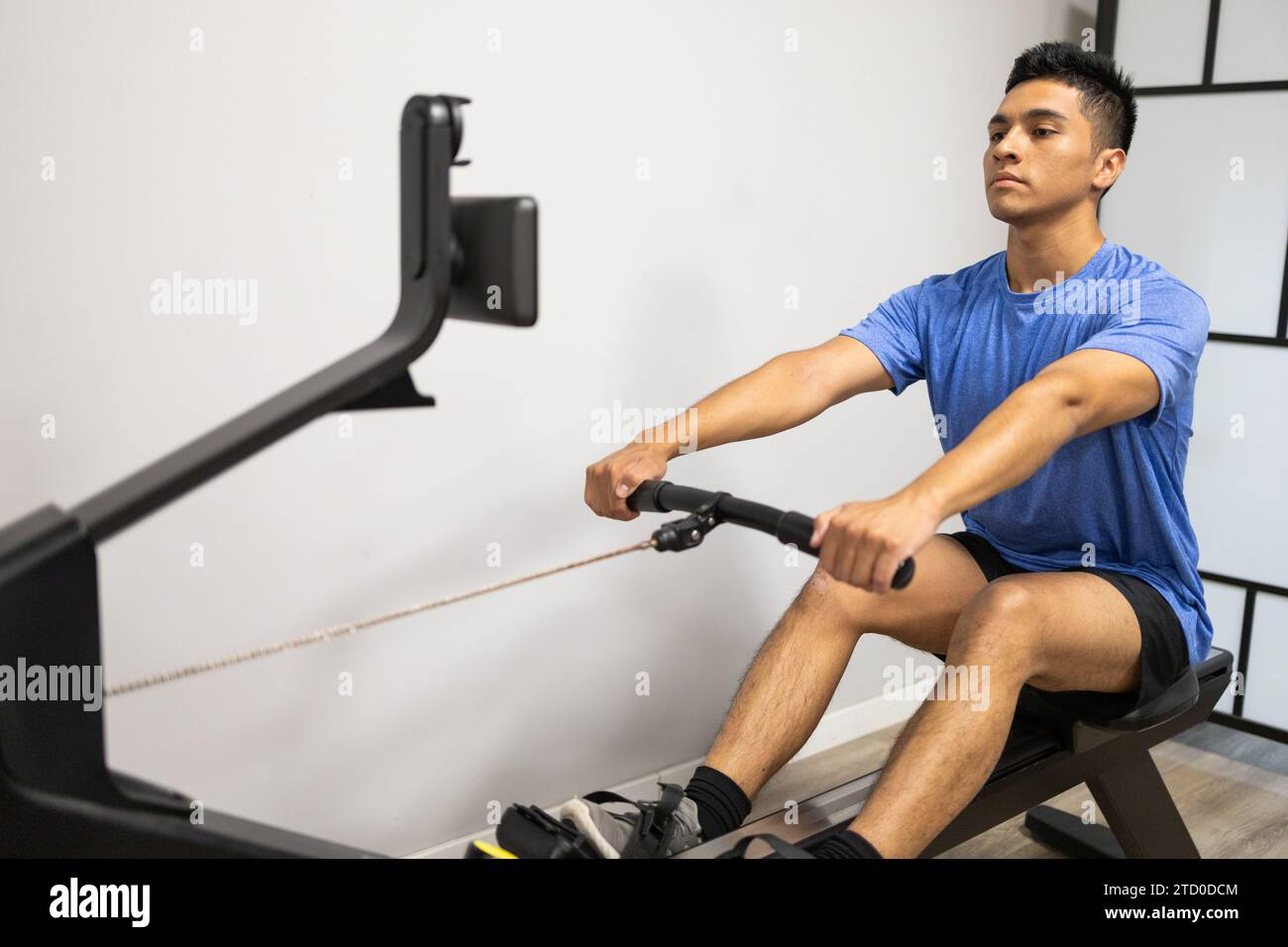 Man in blue shirt using a rowing machine at a gym focused on his ...