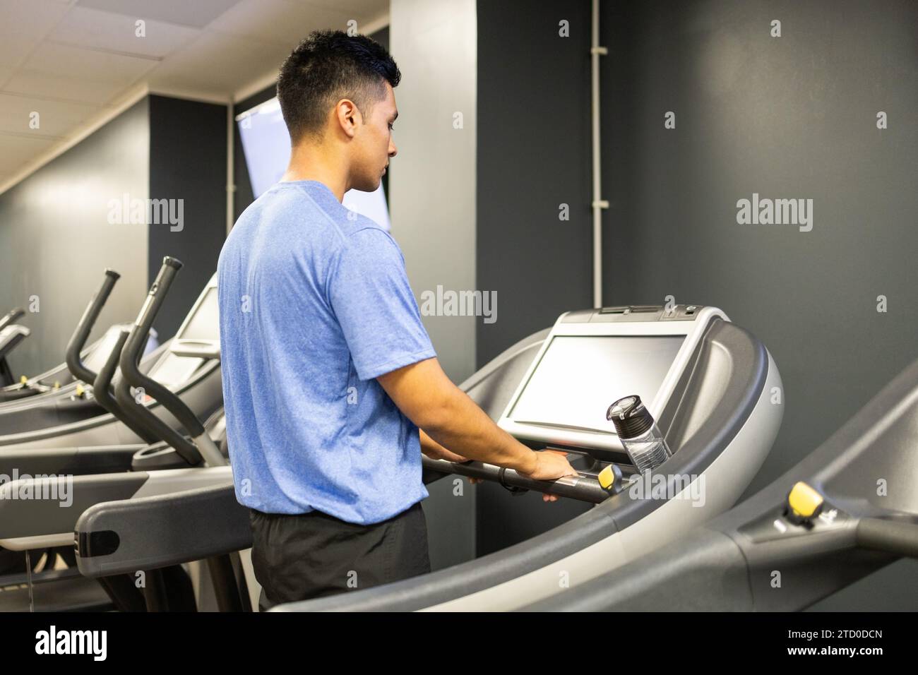 A focused man stands on a treadmill, ready to start his workout routine ...