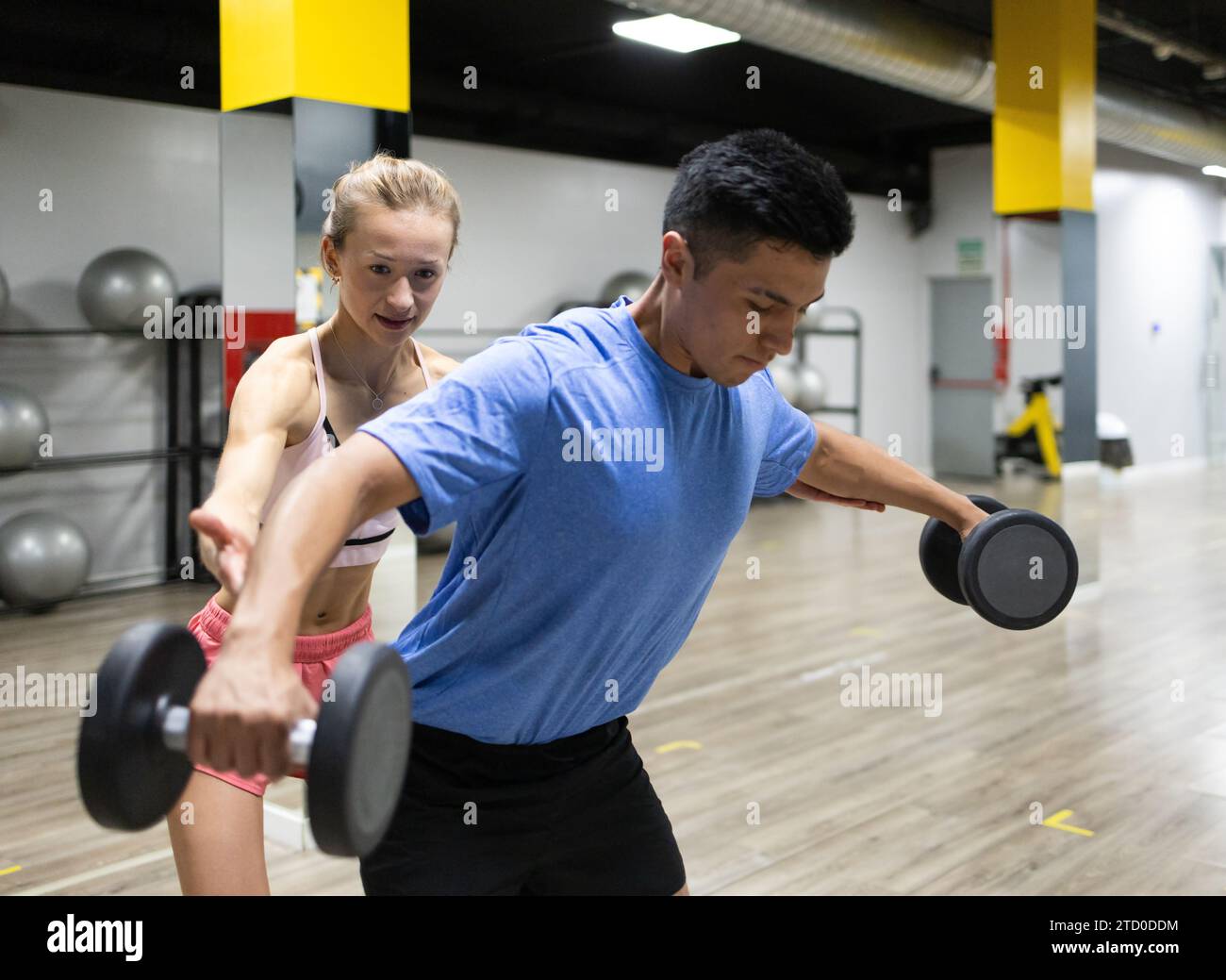 A focused personal trainer guiding a man during a shoulder dumbbell ...