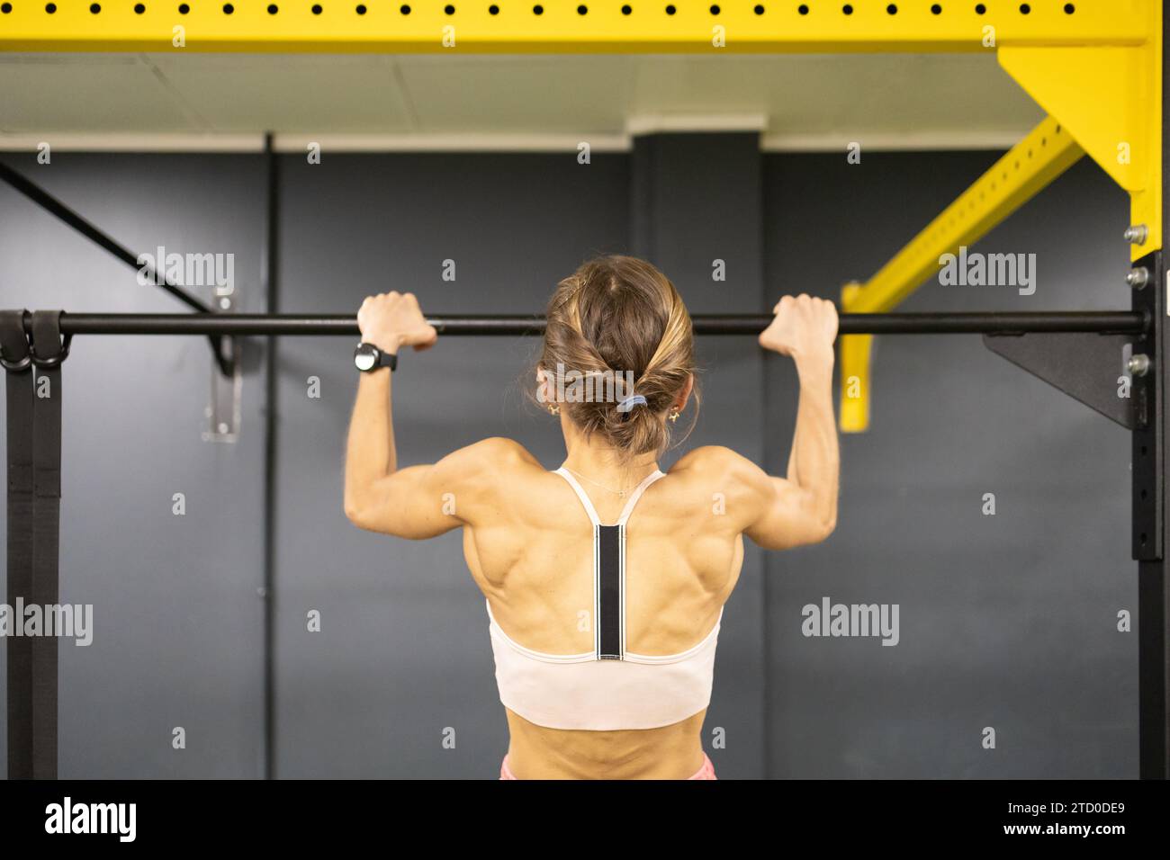 Rear view of a toned woman performing pull-ups on a bar in a fitness ...