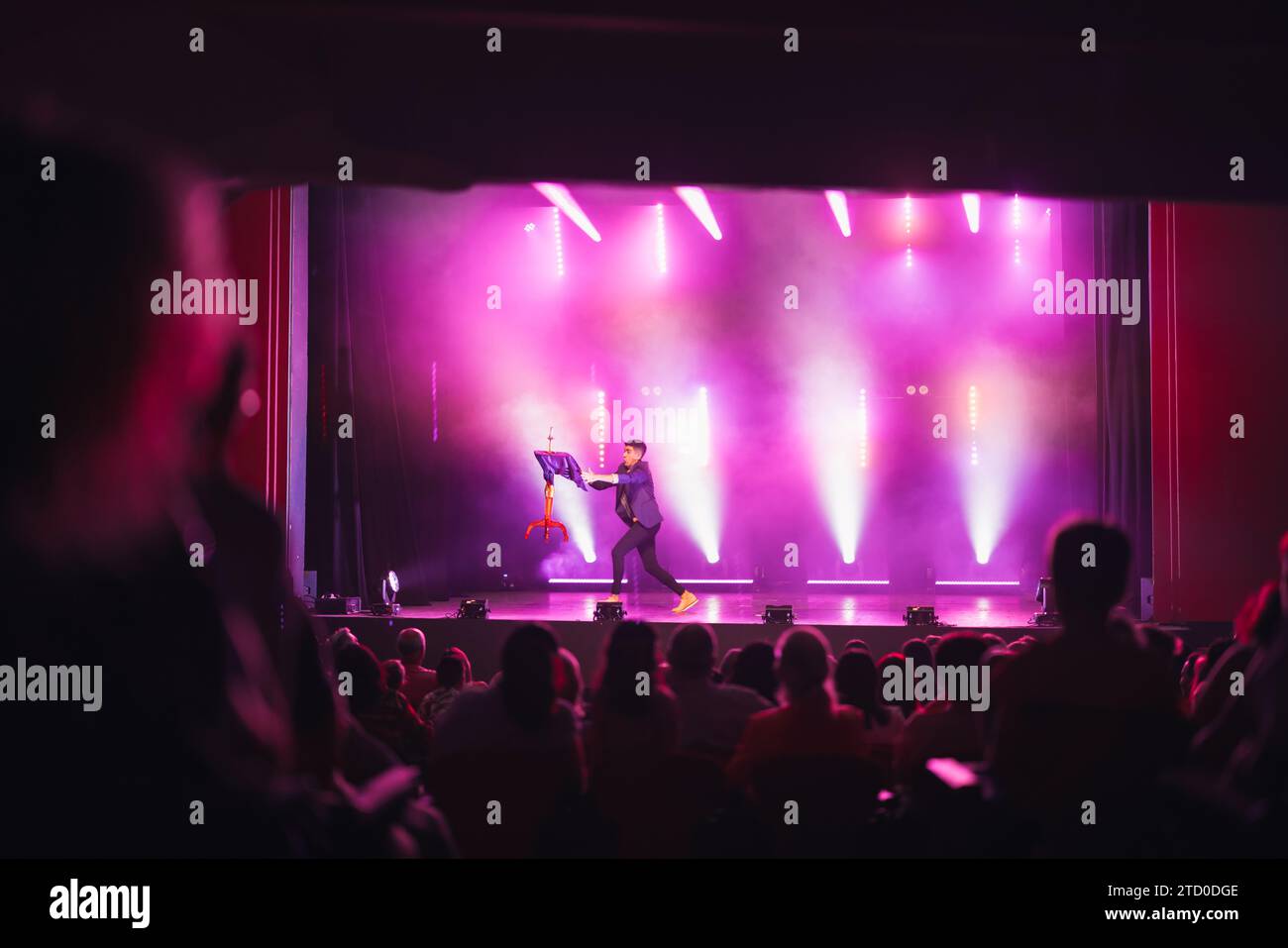 Magician performing magical trick on stage illuminated by pink ...