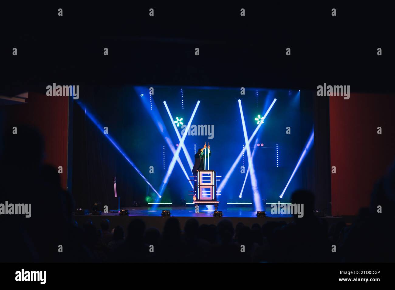 Magician in black suit performing magic trick with boxes on dark stage ...