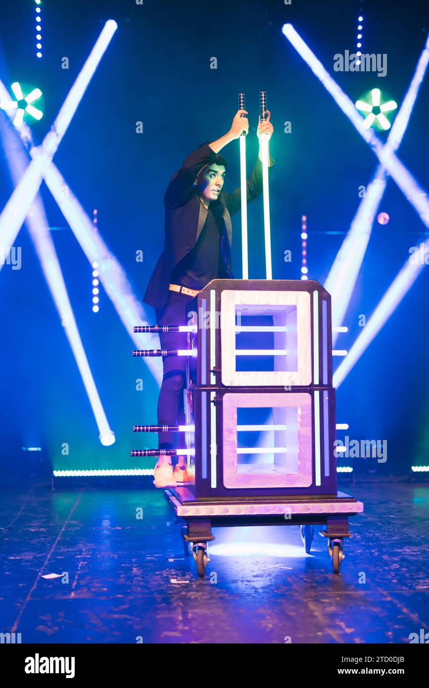 Magician in black suit performing magic trick with boxes on dark stage ...