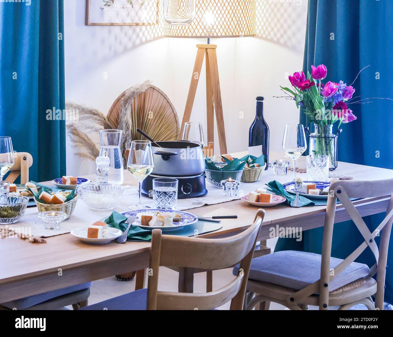 An elegant dinner table is set with a modern fondue pot, wine glasses ...