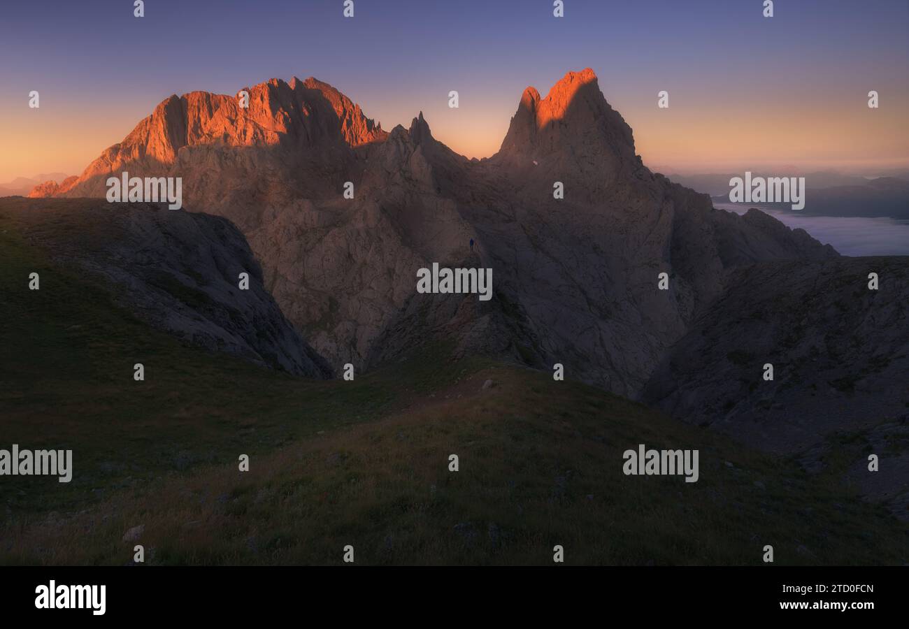 A serene sunset casts glowing light on the rugged peaks of a majestic ...