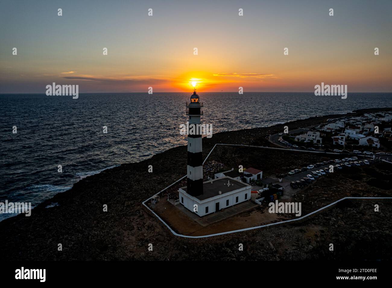 Aerial view of Faro d'Artrutx at sunset, with the sun dipping into the ...
