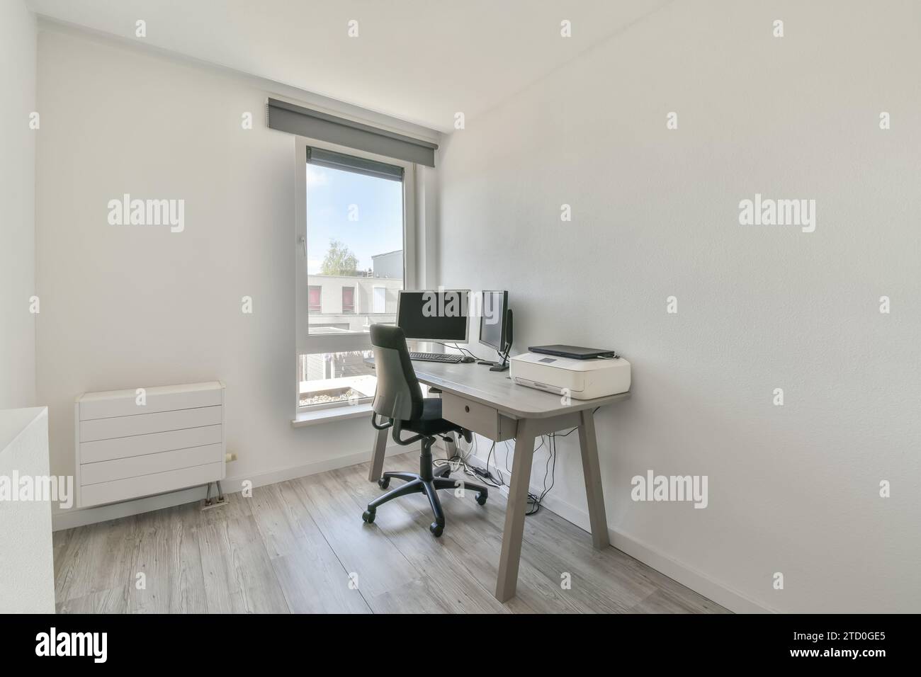 Computers and printer on desk with empty chair by window in home office ...