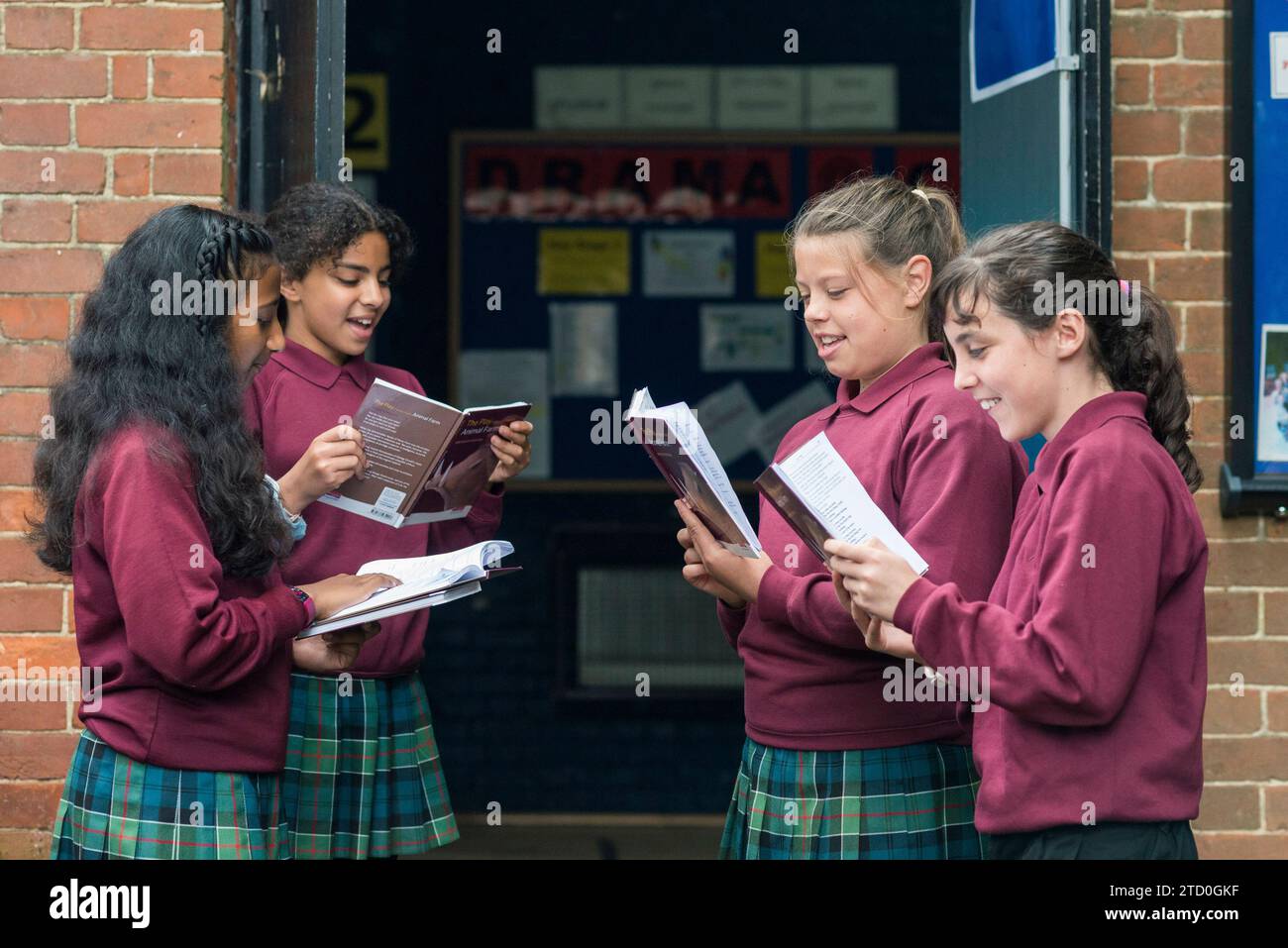 A group of girls stand outside a classroom reading and rehearsing a ...
