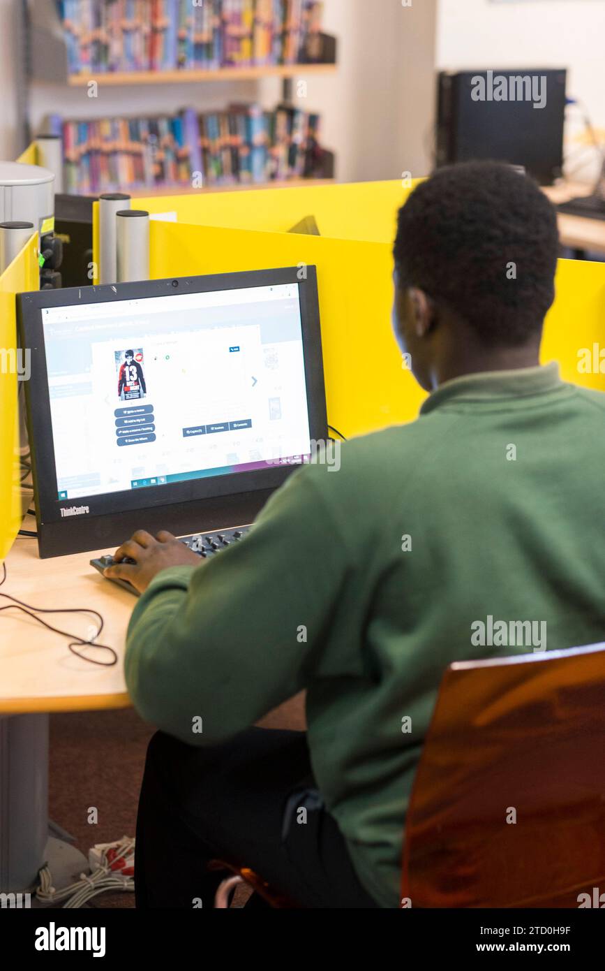 A boy in school uniform sits at a computer in a school library Stock ...