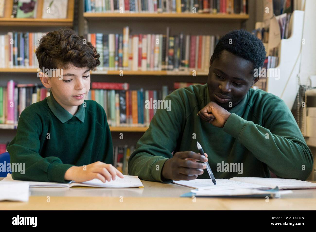 Two boys sit at a desk and work together studying from their workbooks ...