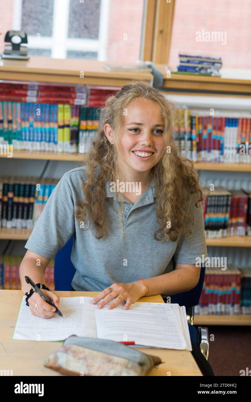 A female A level student sits at a desk in a school library revising ...