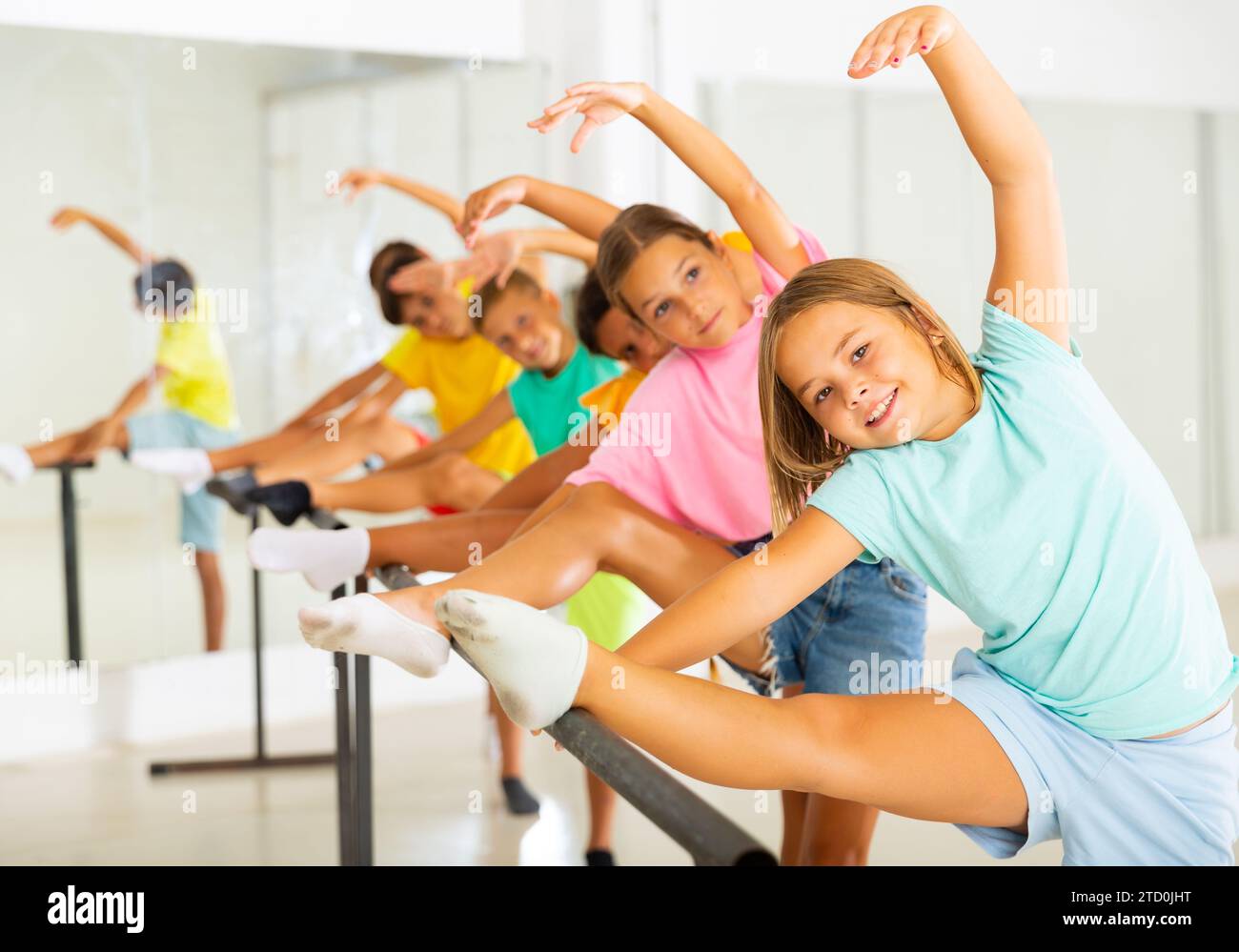 Cheerful girl working near ballet barre during group choreography class ...