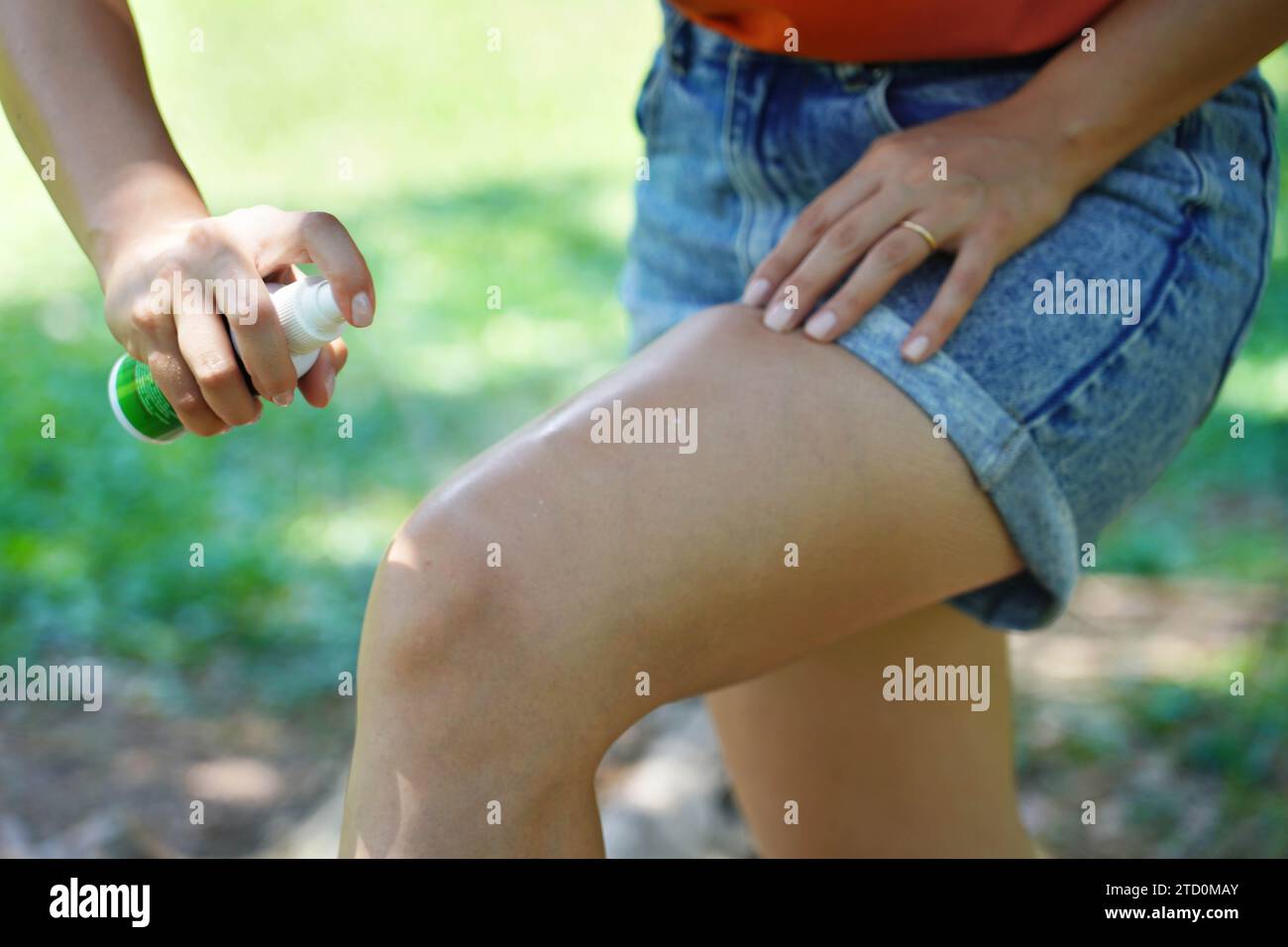 Close-up of young woman applying insect repellent onto leg in park ...