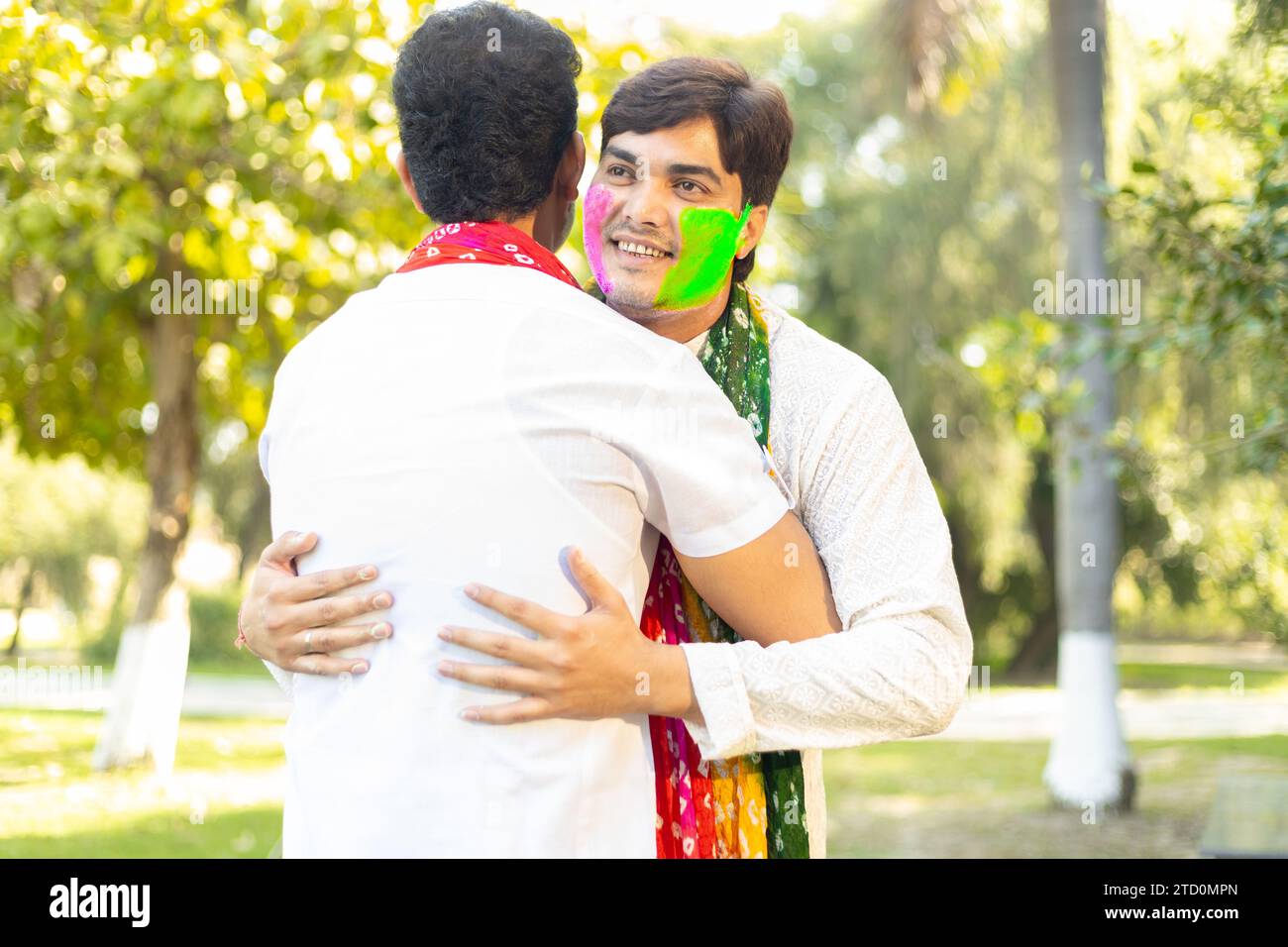 Two young indian men wearing white kurta greeting, hugging each other ...