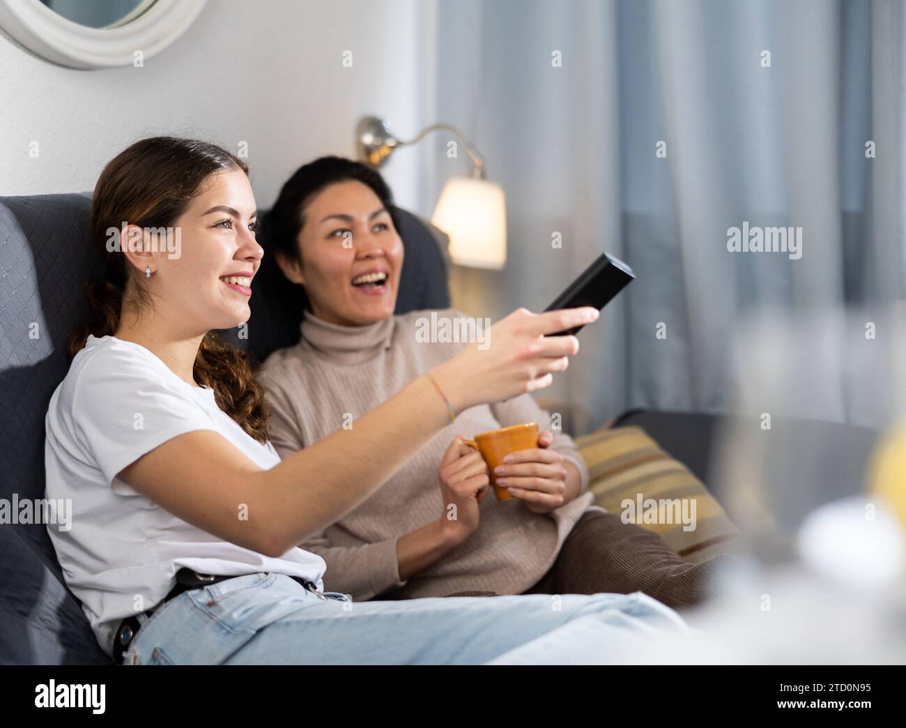 Positive women sitting on couch and watching TV together Stock Photo ...