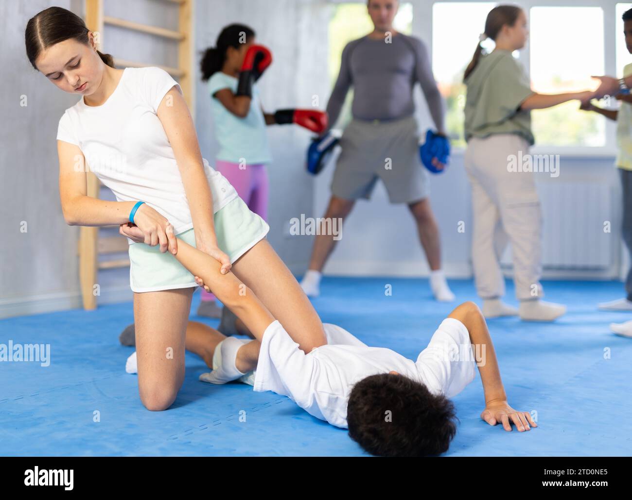 Tween girl applying armlock to face-down boy in mock fight at self-defense classes Stock Photo ...
