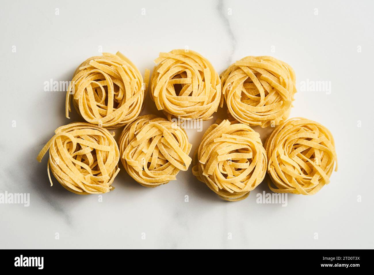 Dry tagliolini or tagliatelle pasta in nests in the bowl on white ...