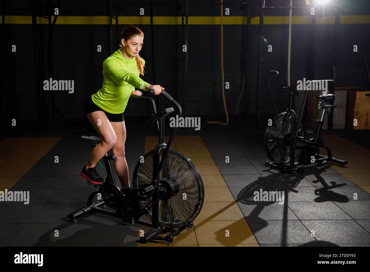 A young muscular woman is doing hard bike crossfit training in the gym ...