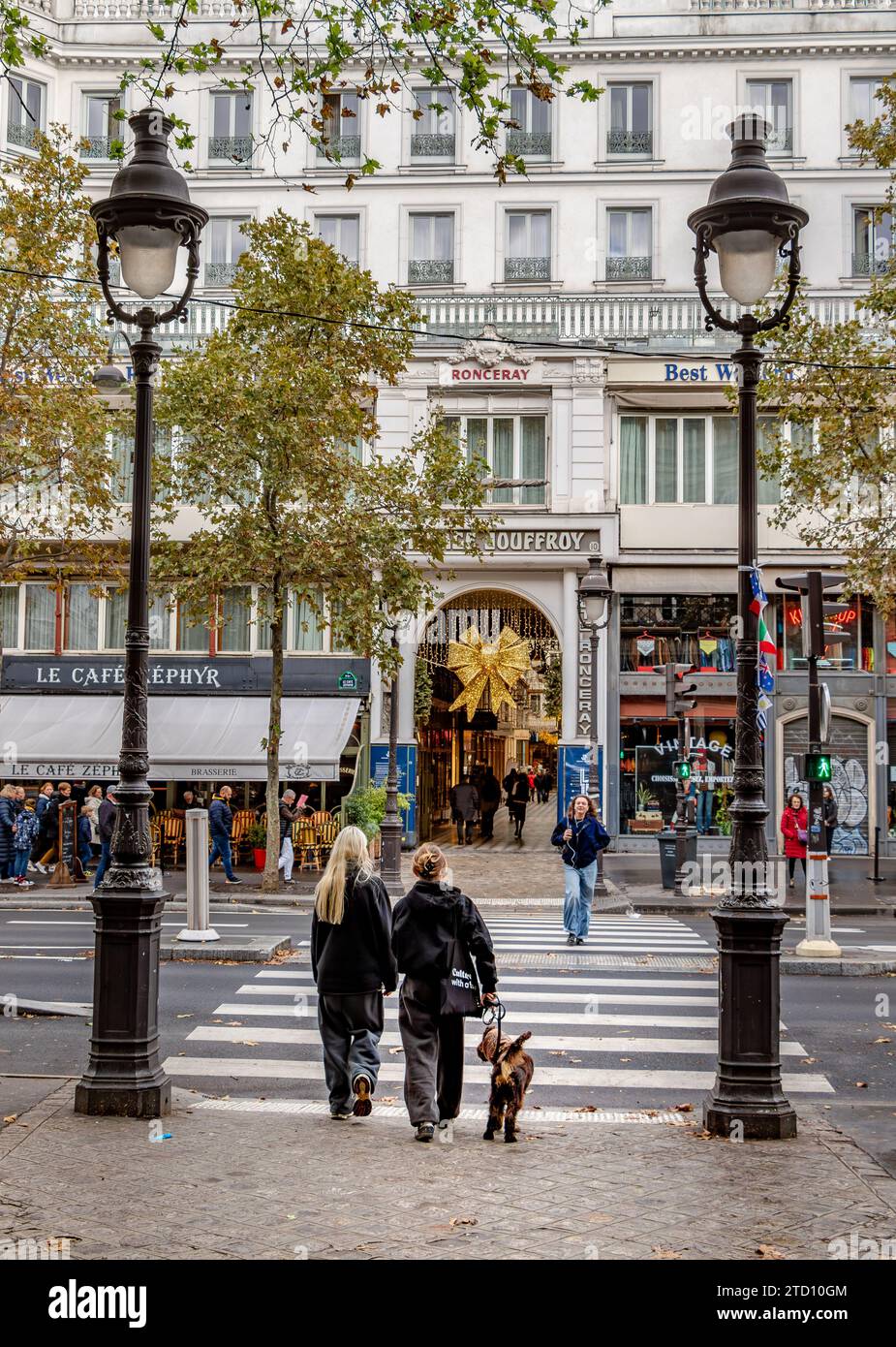 Two woman & a dog crossing the road at the entrance to Passage Jouffroy ...