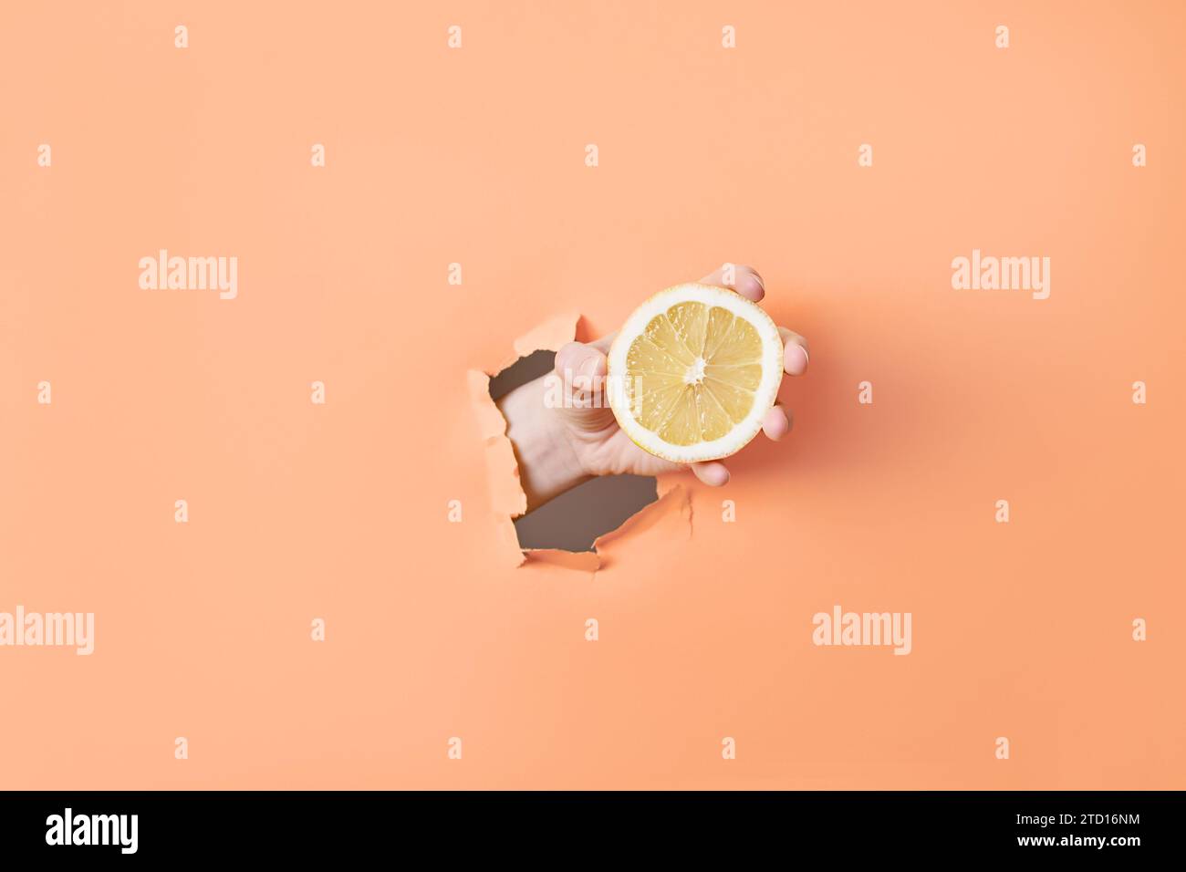 Female hand holding lemon through the hole in peach fuzz background ...