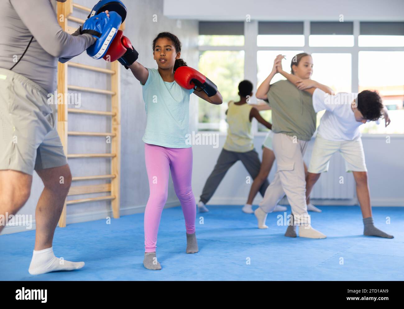 Black tween girl in boxing gloves punching pads in hands of coach Stock ...