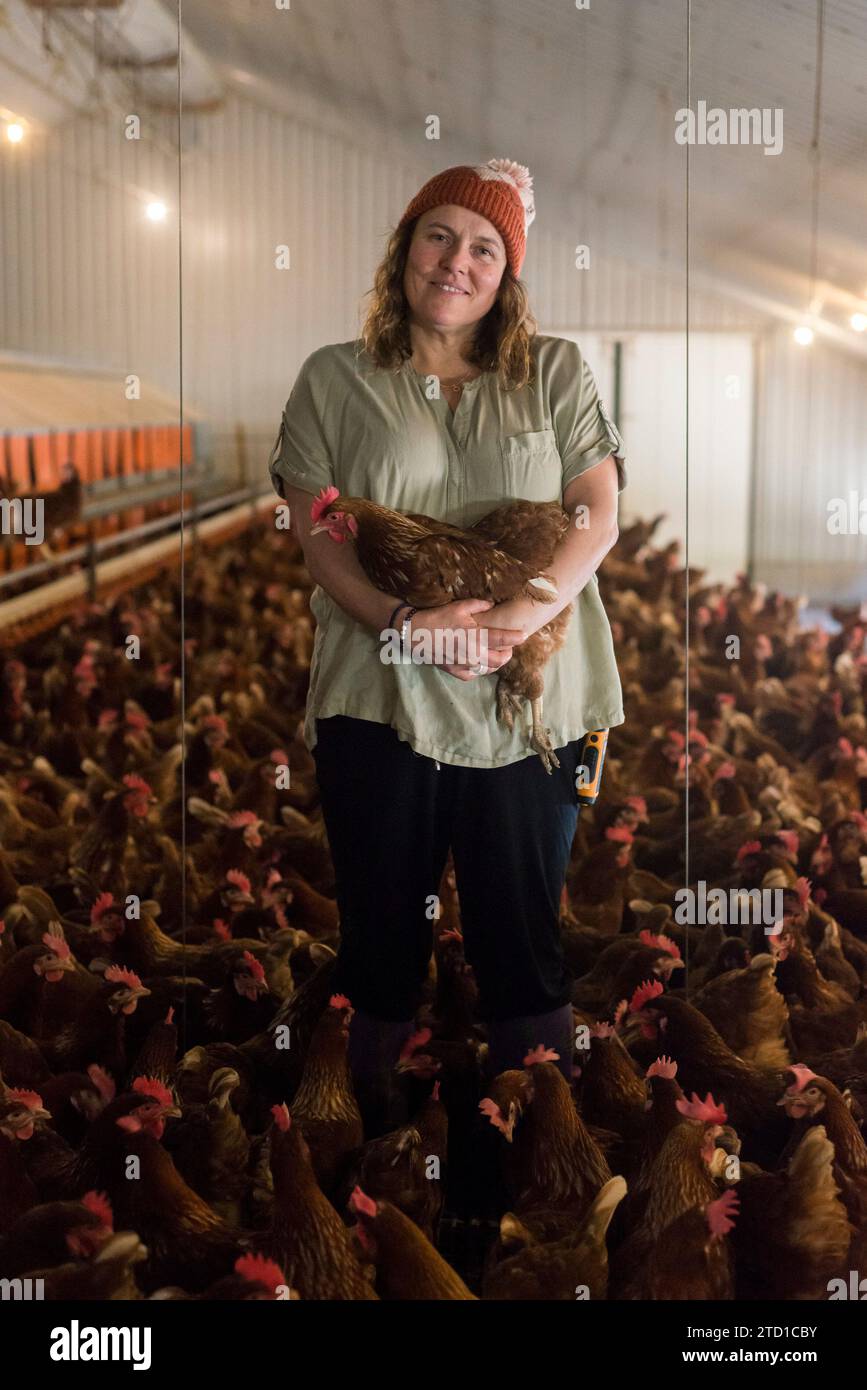 A female farmer stands holding a chicken surrounded by a flock of ...