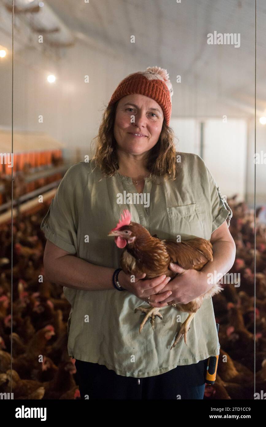 A female farmer stands holding a chicken surrounded by a flock of ...