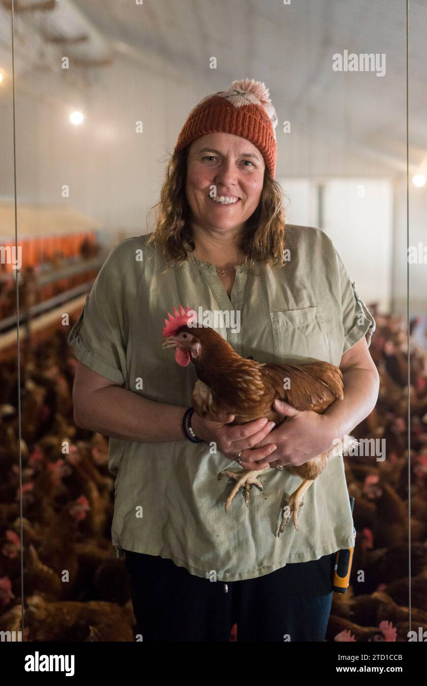A female farmer stands holding a chicken surrounded by a flock of ...