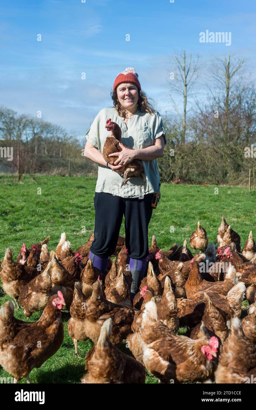 A female farmer stands holding a chicken surrounded by a flock of ...