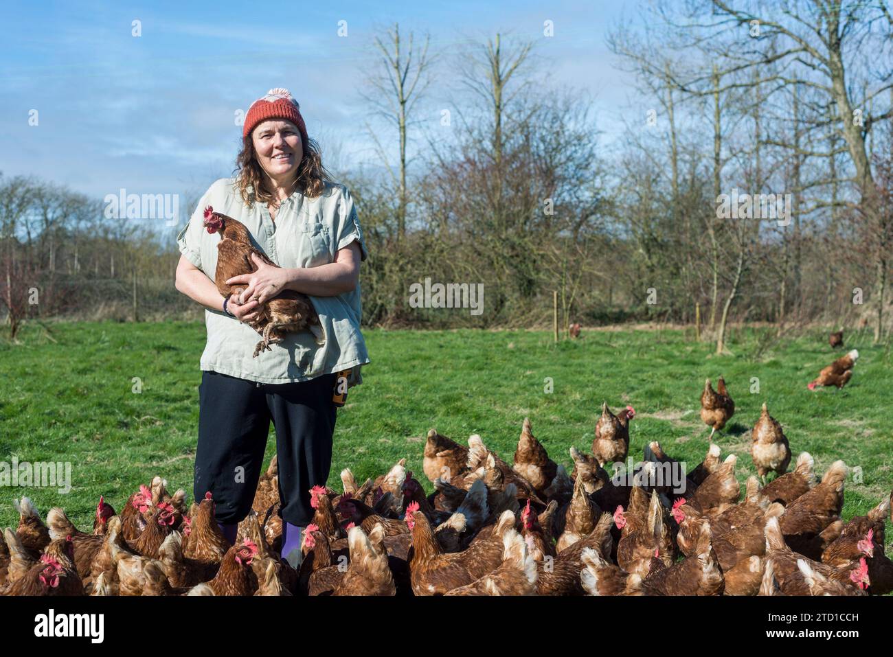 A female farmer stands holding a chicken surrounded by a flock of ...