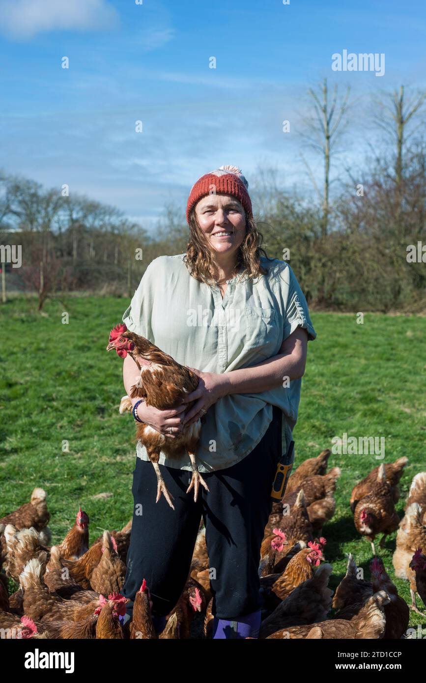 A female farmer stands holding a chicken surrounded by a flock of ...