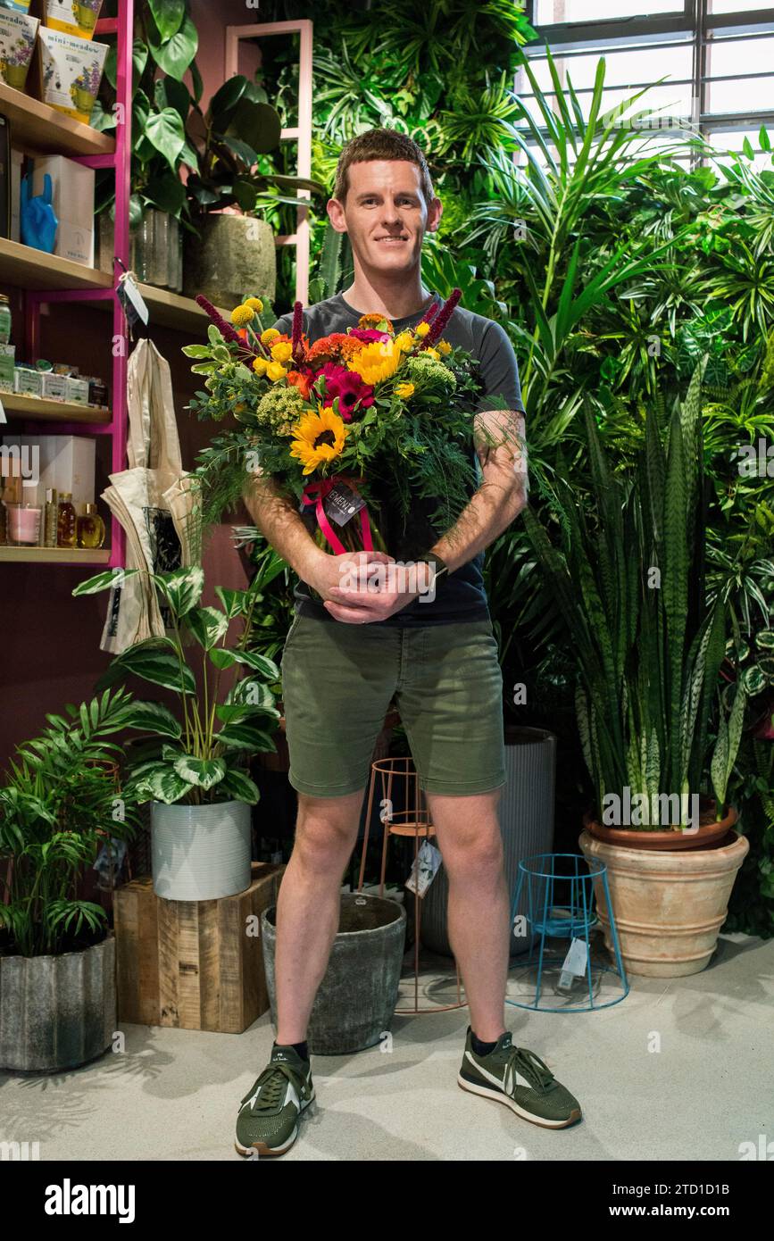 A small business owner of a florist shop stands with a bouquet of ...