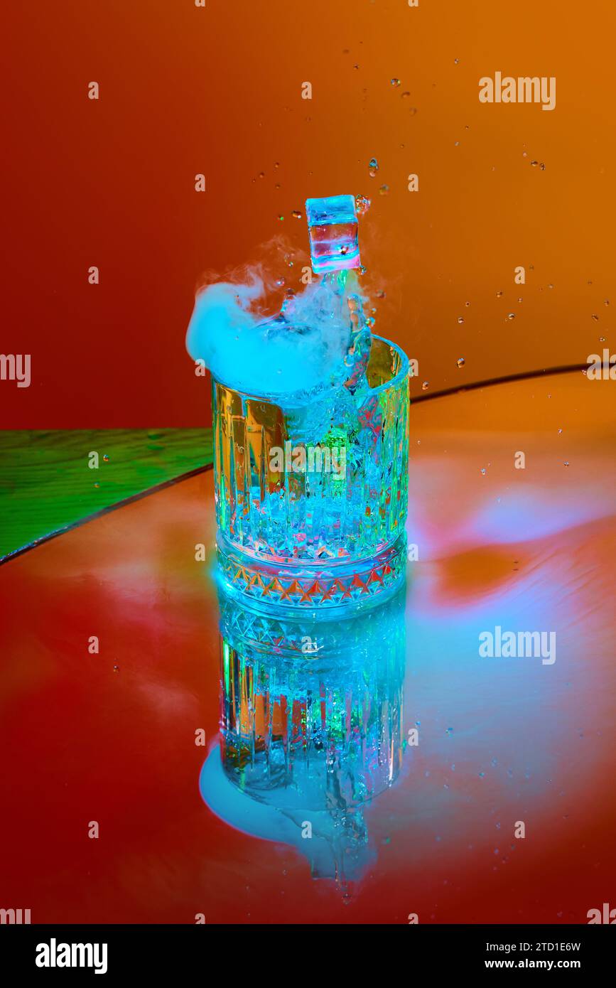 Ice cube falling down into glass with alcohol against orange background ...