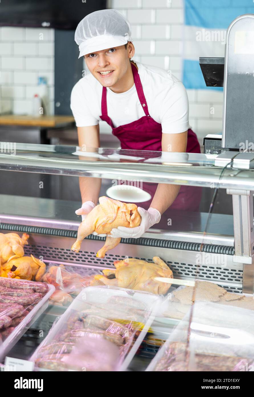 Positive young salesman demonstrating chicken in butcher shop Stock ...