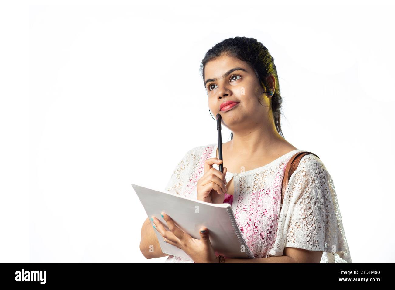 A pretty young Indian girl thinking while taking notes and looking ...